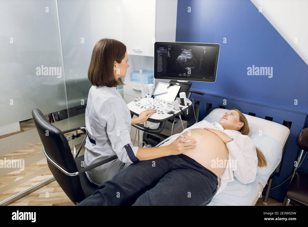 Pregnant woman getting ultrasound sonogram scan, while young ...