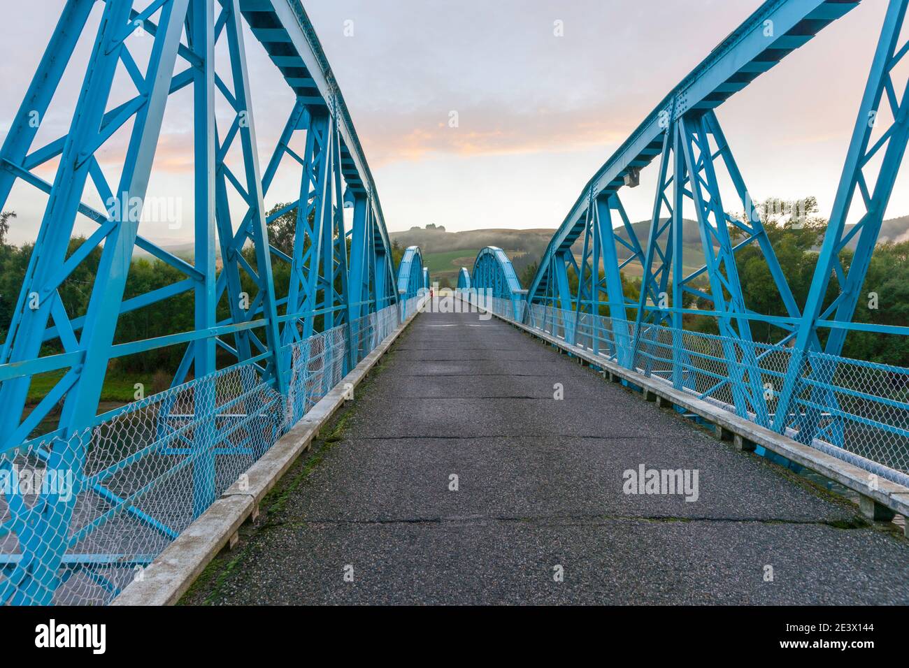 Long straight road between steel arches of bridge leading to distant ...