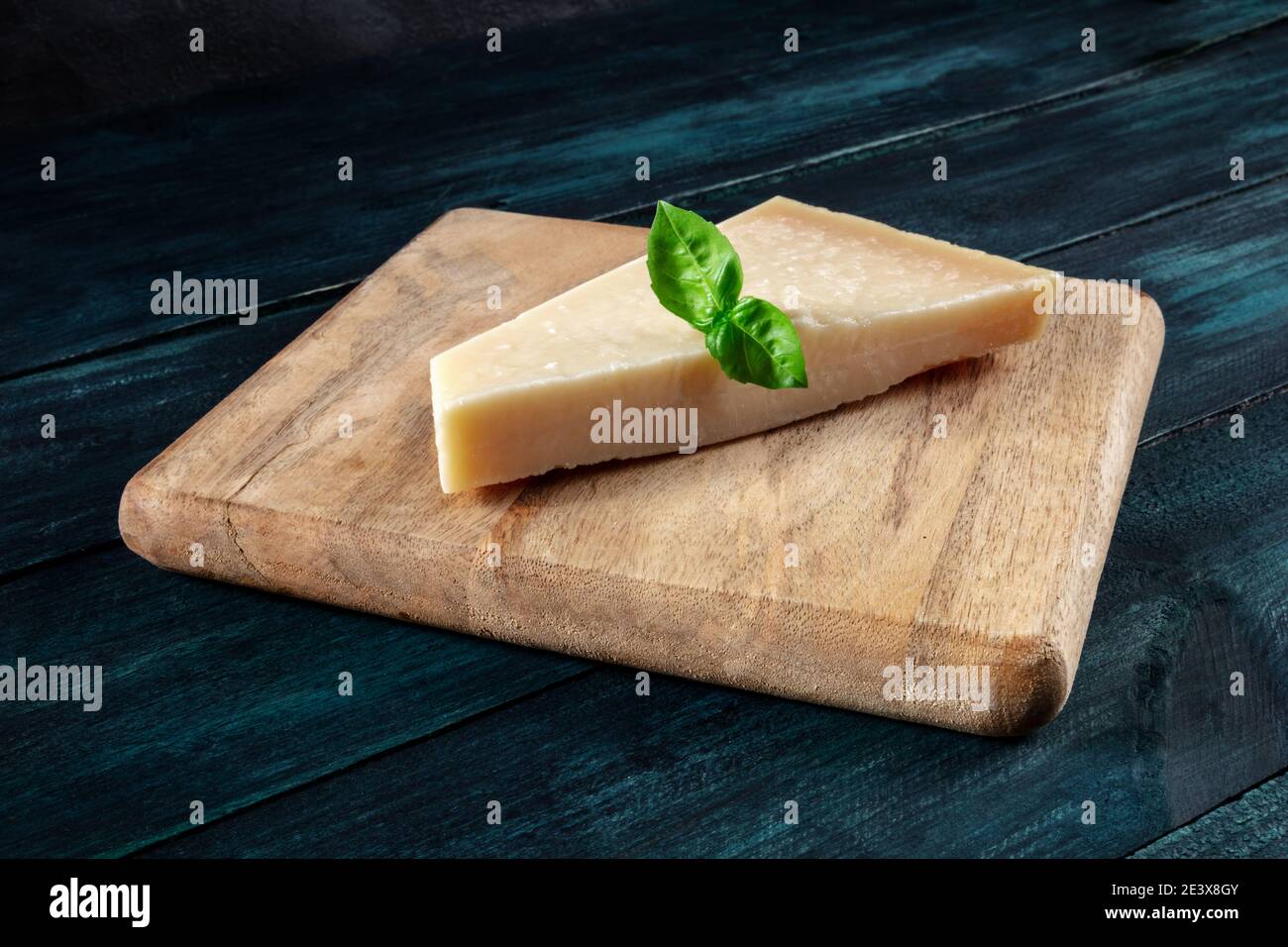 Parmesan cheese with basil leaves, on a wooden cutting board on a dark ...