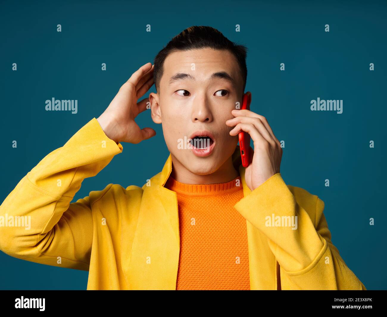 surprised asian man on blue background talking on the phone and holding ...