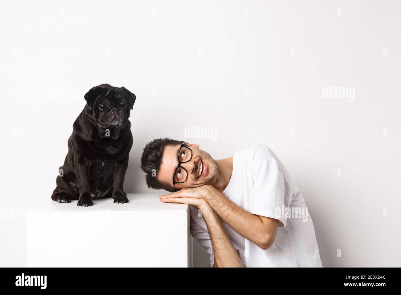 Handsome young man lay head near cute black pug, smiling and looking up ...