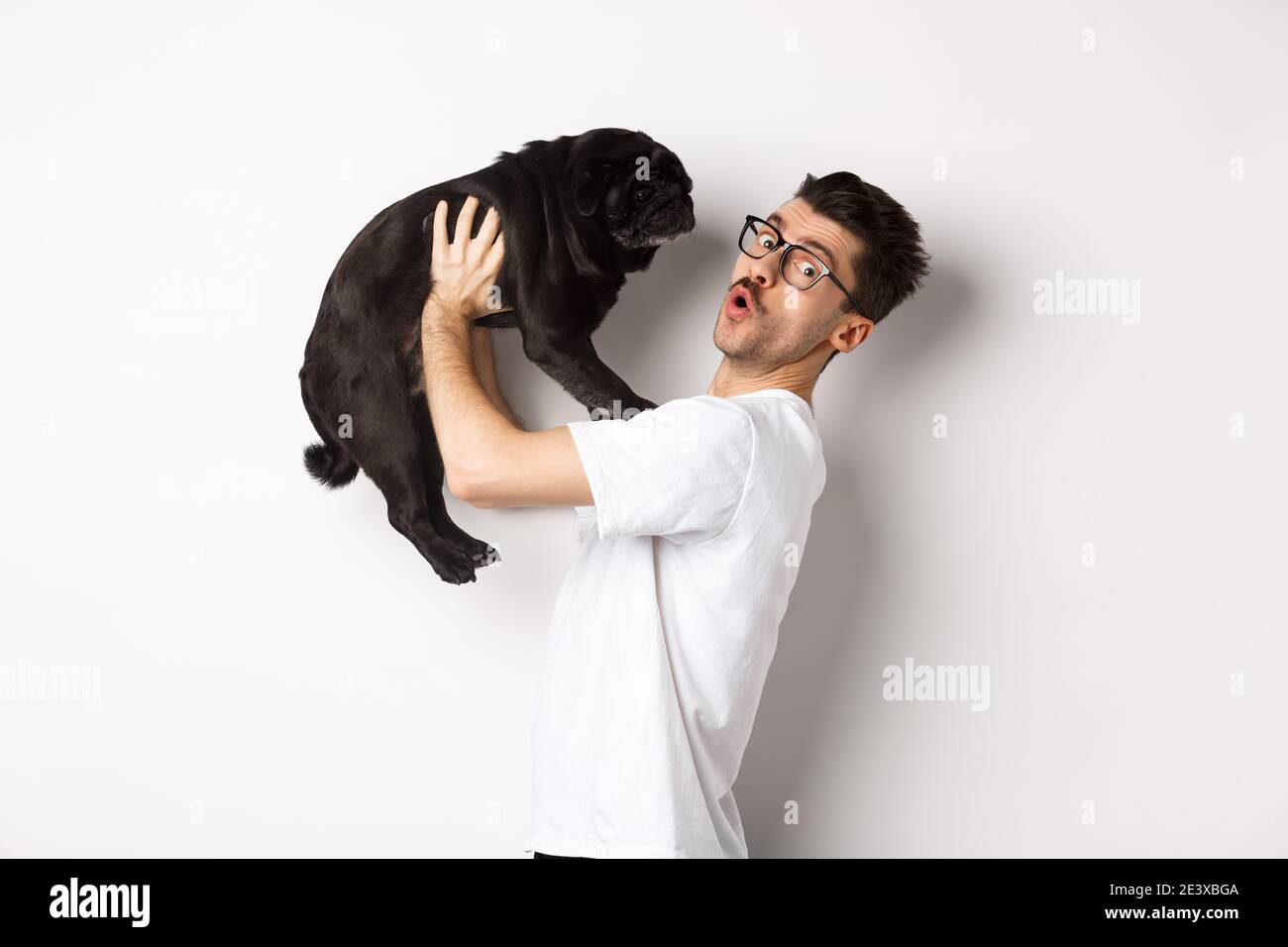Image of handsome young man loving his pug. Dog owner holding puppy and ...