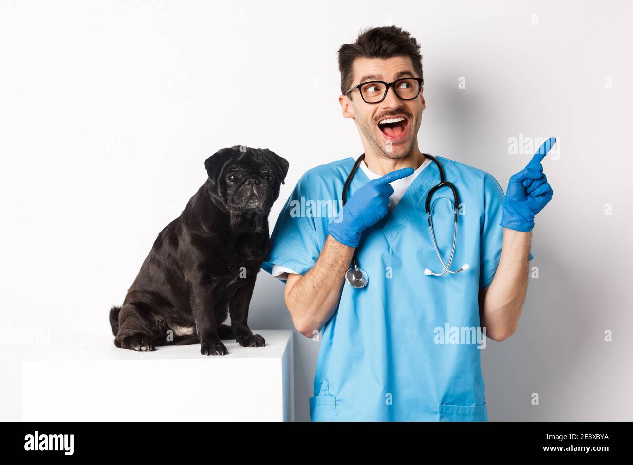 Handsome young doctor at vet clinic pointing fingers upper right corner ...