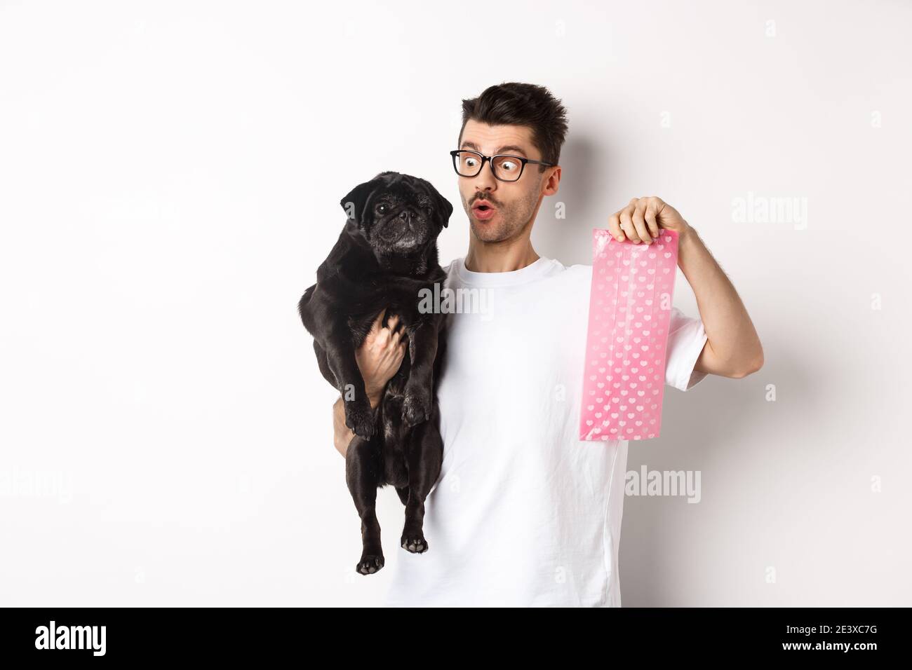 Cheerful young man holding black pug and pink dog poop bag, standing ...