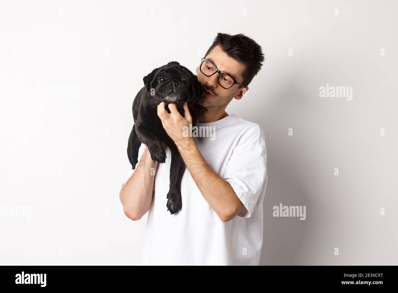 Handsome young man pet his cute black dog, scratching pug while holding ...