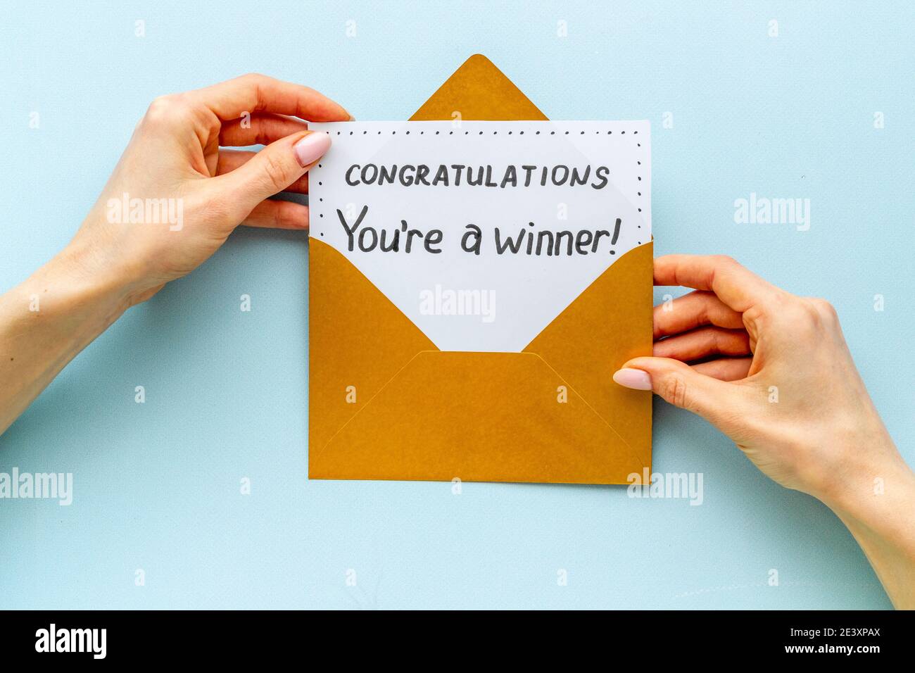 Hands holding award congratulation card in golden envelope. Text You're ...