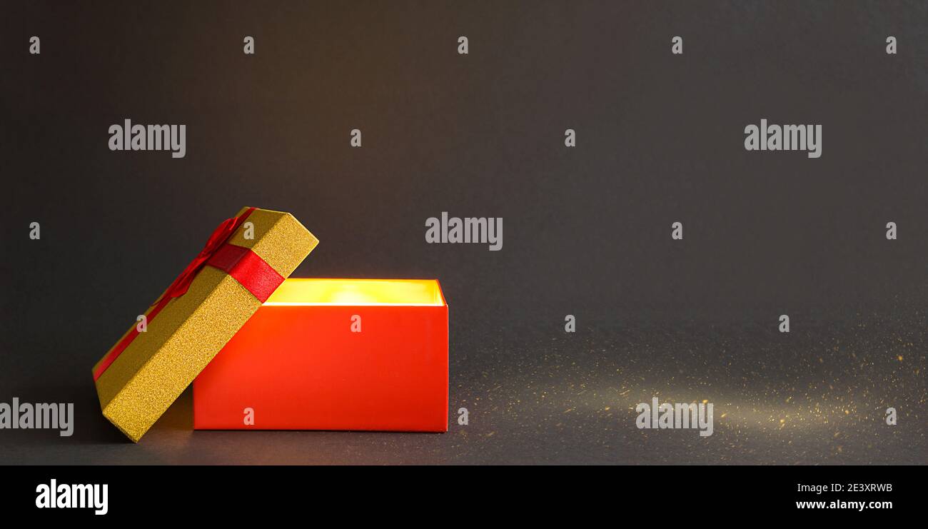 Open red gift box with a bow with a golden glow and glitter inside on a ...