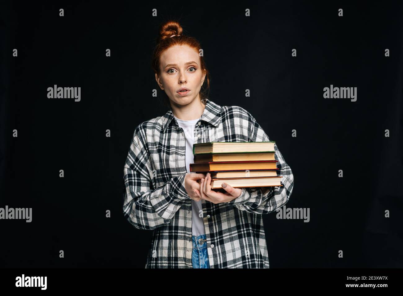 Shocked young woman college student holding books and looking at camera ...
