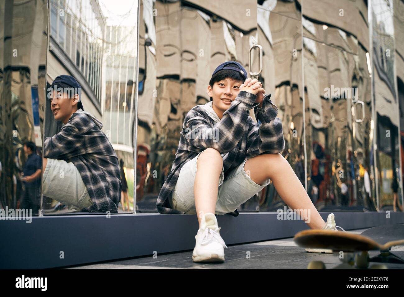 teenage asian kid skateboarder taking a break sitting on ground smiling ...