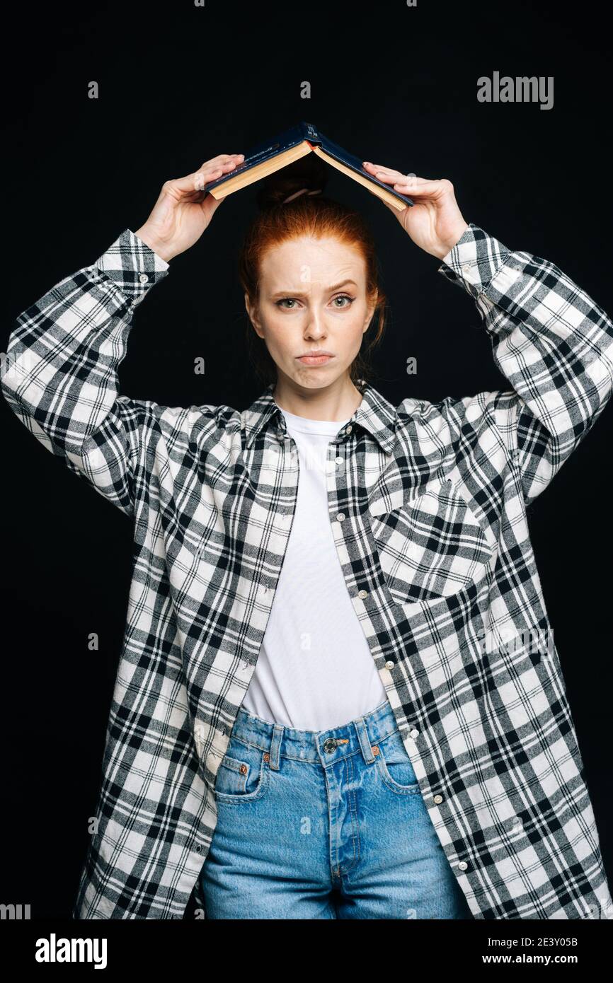 Negative confused young woman college student holding book over head ...