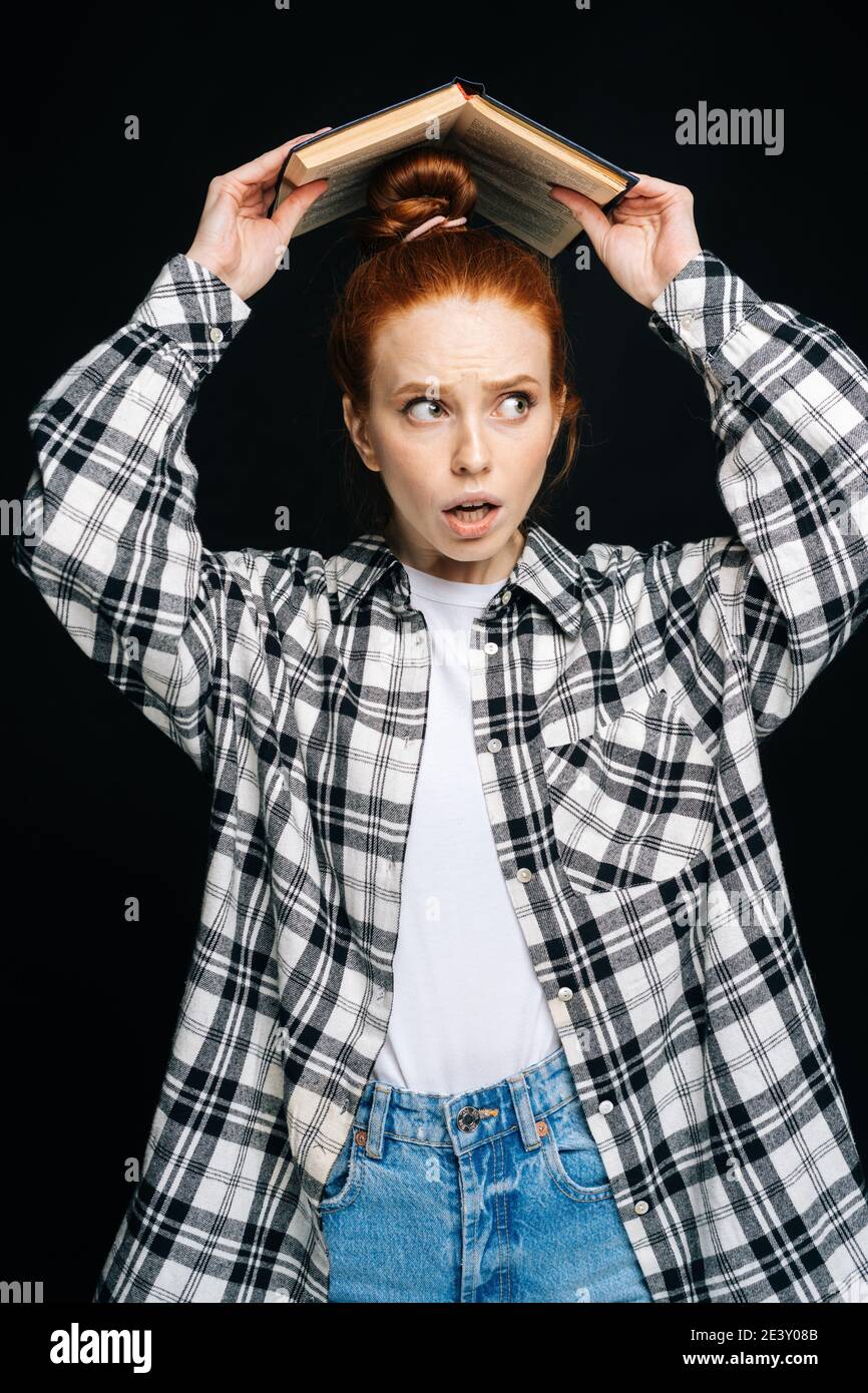 Shocked young woman college student holding book over head and looking ...