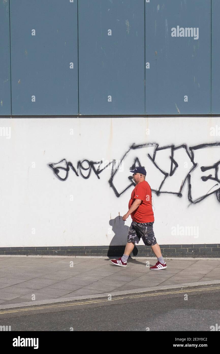 A male holidaymaker walking past a wall sprayed with ugly graffiti tags ...