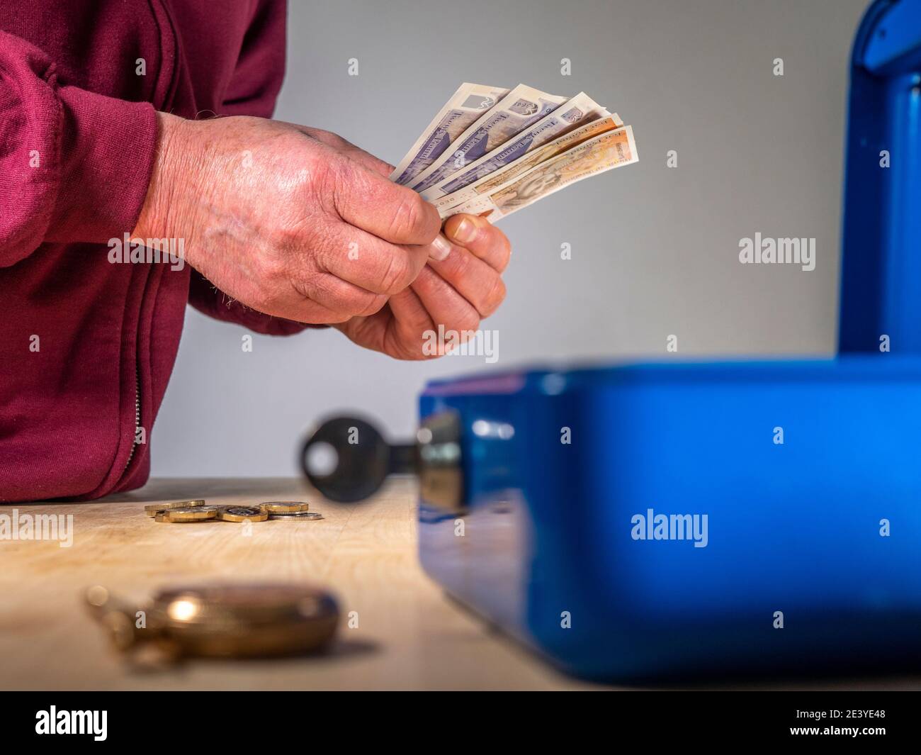 A man’s hands holding sterling pound currency notes, with coins below ...