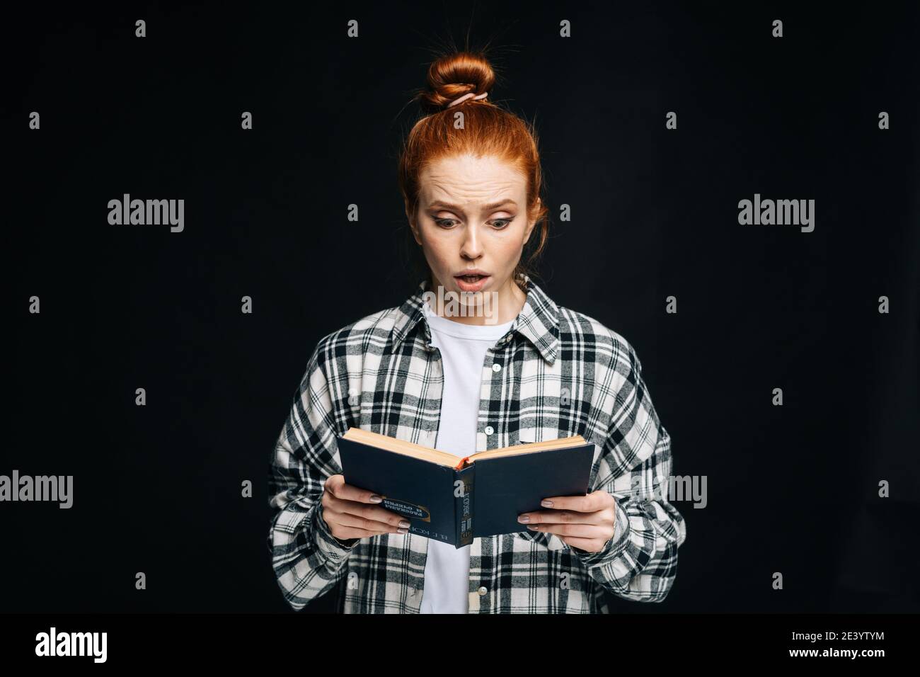 Shocked young woman college student reading book on black isolated ...