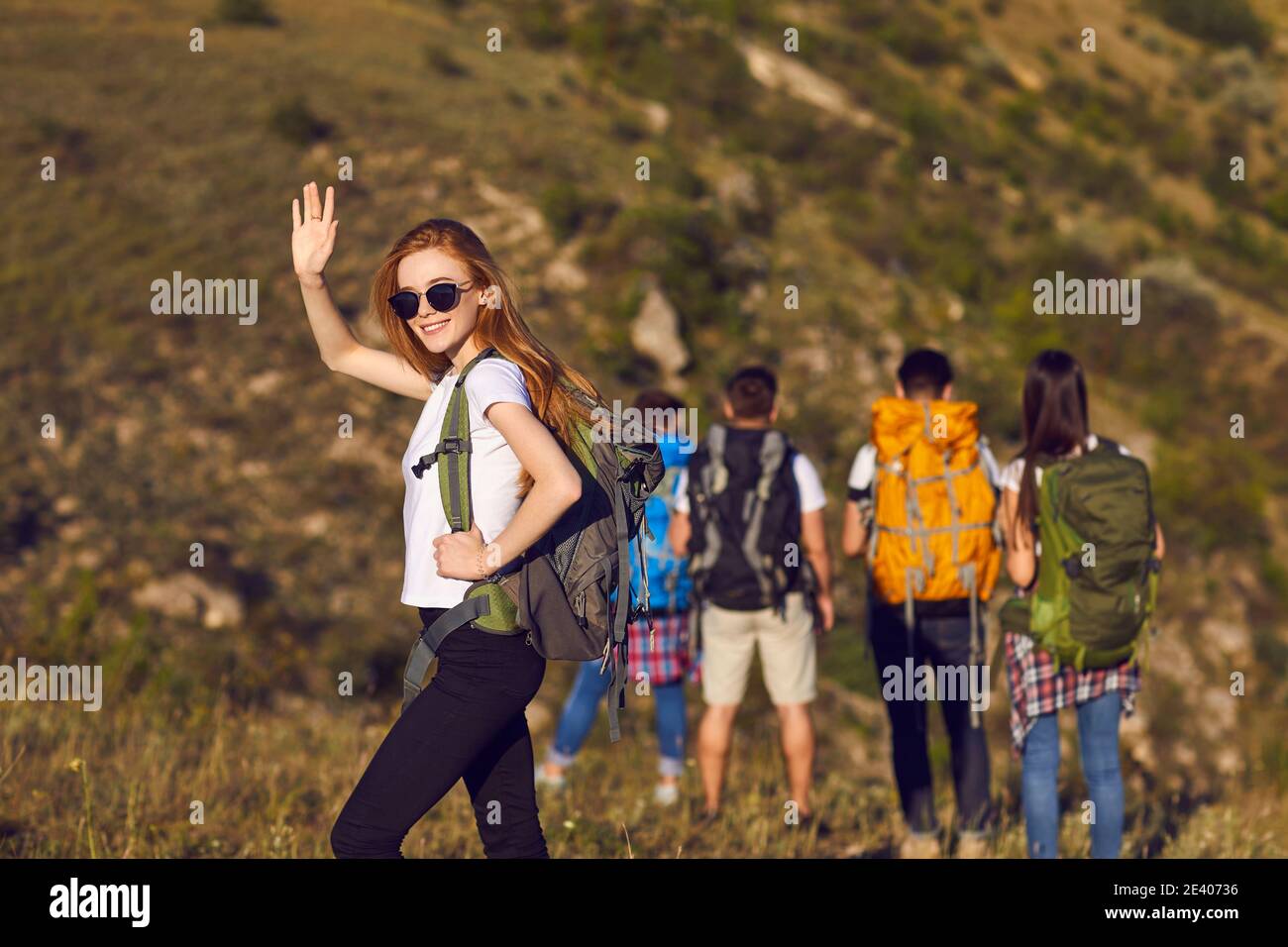 Smiling girl tourist hiker with backpack standing and waving with hand ...