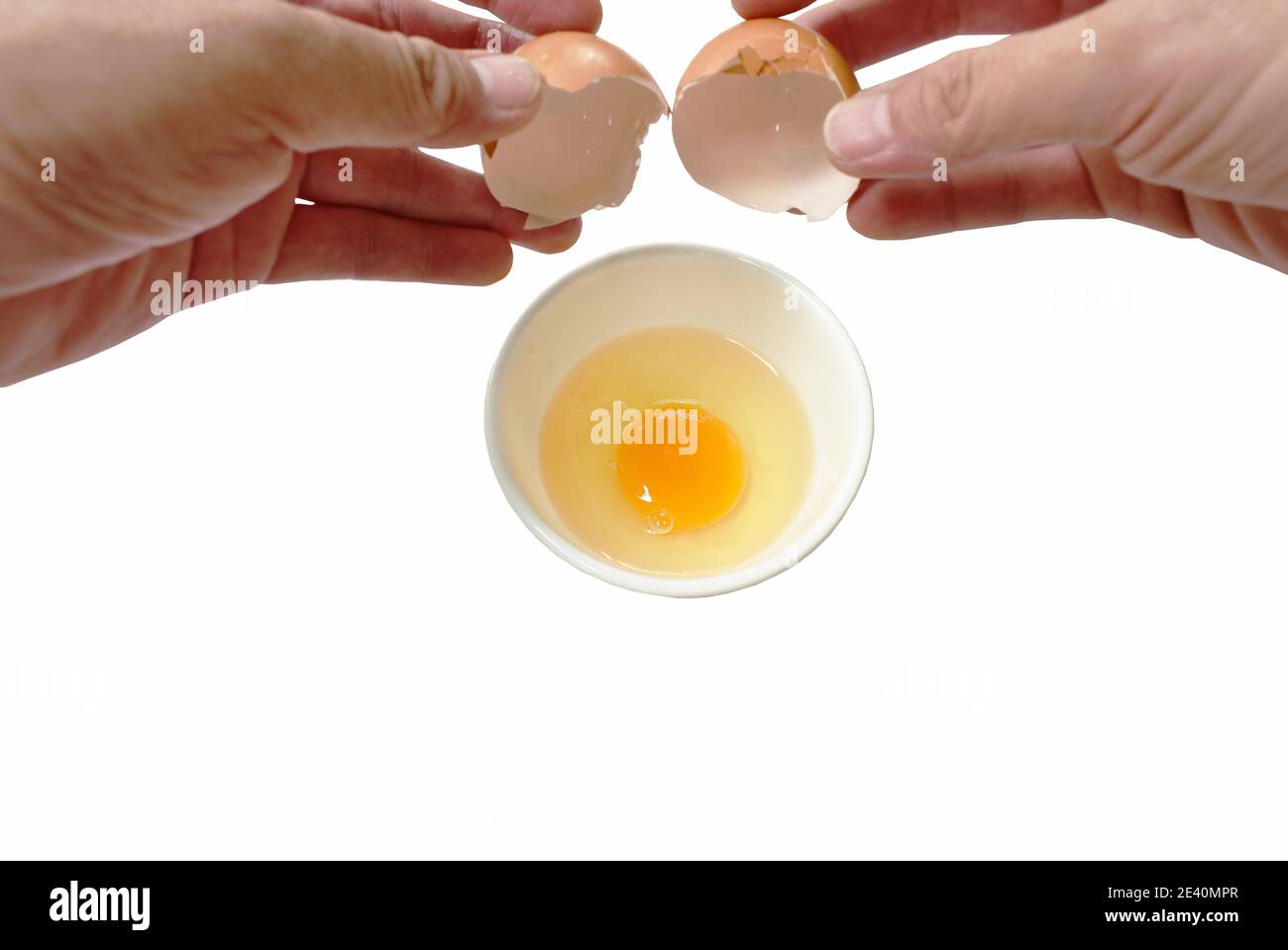 hand opened shell and raw egg with yolk dropping in cup on white ...