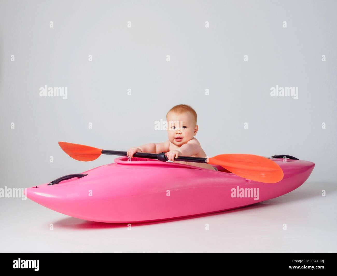 Studio shot of a baby sitting in a pink Kayak with an orange paddle, on ...
