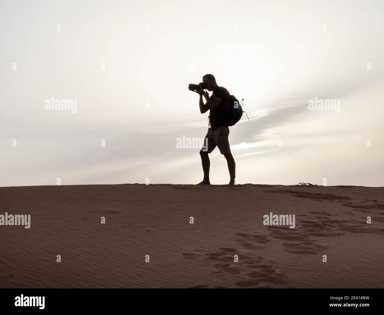 A young man taking pictures with his camera on top of a dune in the ...