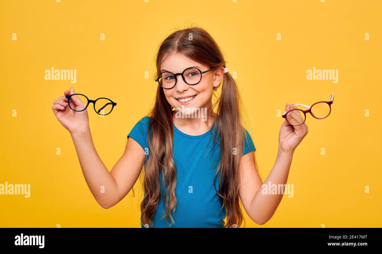 Vision correction with child's eyeglasses. Funny girl wearing glasses holding stylish eyeglasses ...