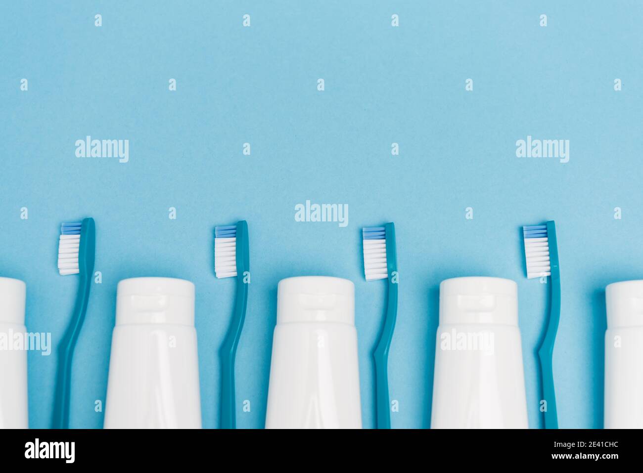 Top view of row of toothbrushes and tubes with toothpaste on blue ...