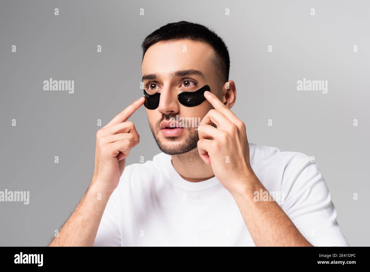young hispanic man applying eye patches isolated on grey Stock Photo ...