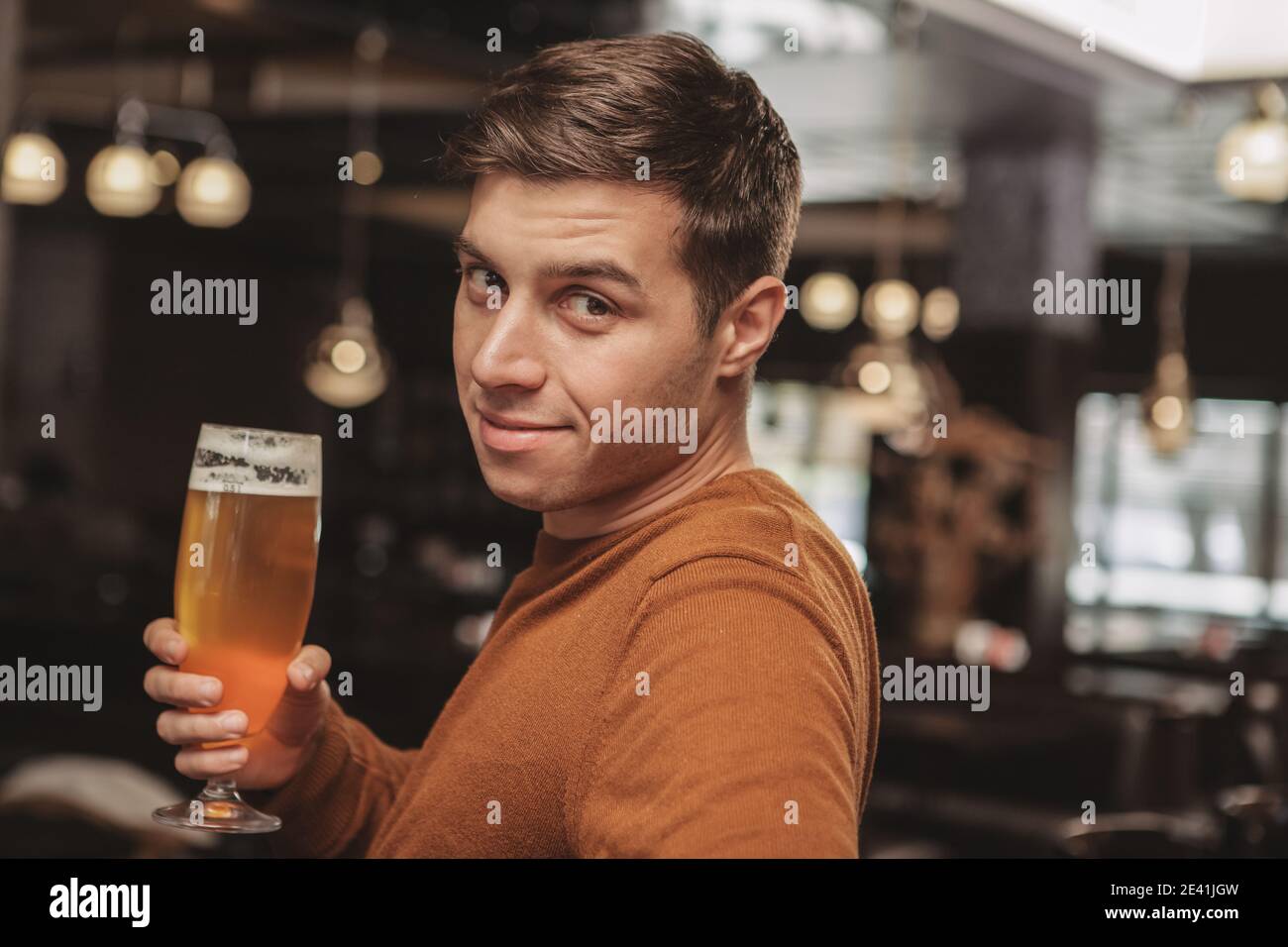 Charming young man smiling to the camera over his shoulder, having ...