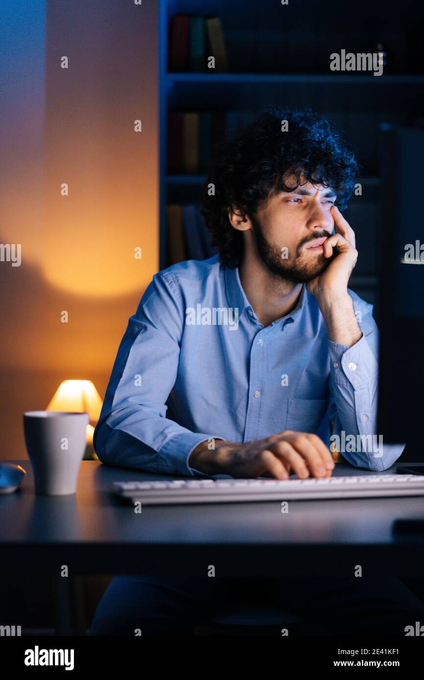 Close-up face of sleepy man working late at night on computer rubbing ...
