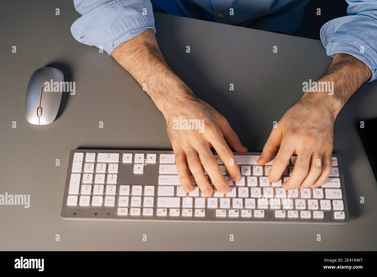 Top View Of Hands Of Unrecognizable Man Using Wireless Keyboard And Computer Mouse At Dark Room