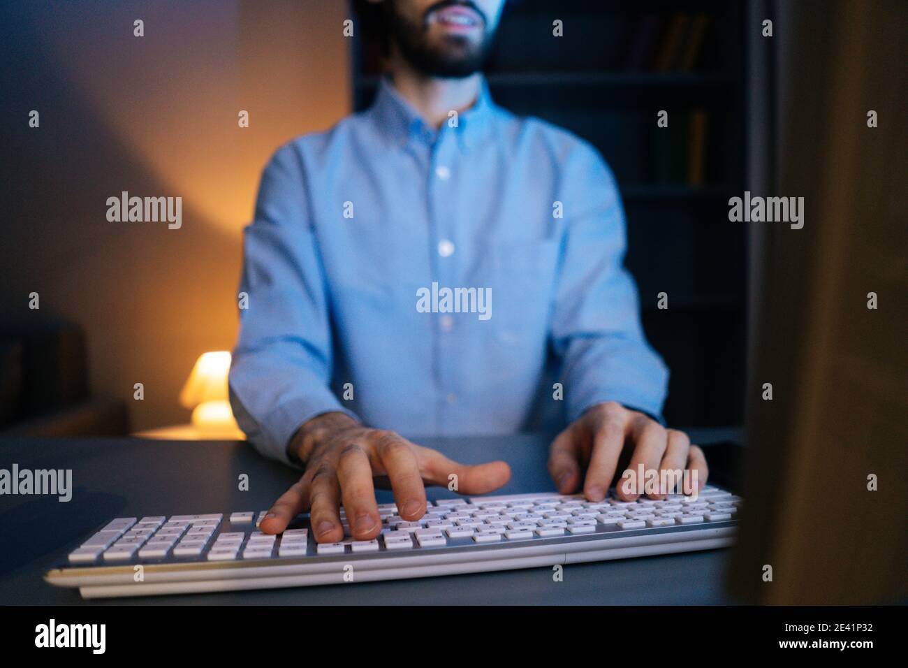 Close-up view of hands of unrecognizable man using computer typing message on wireless keyboard ...