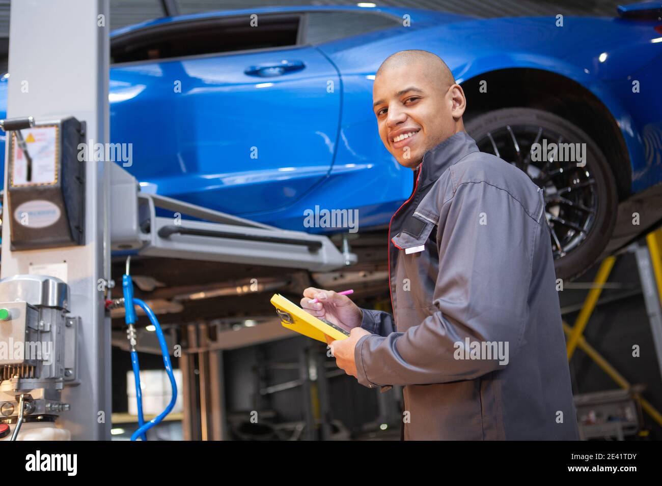 Charming male car service worker smiling to the camera while taking ...