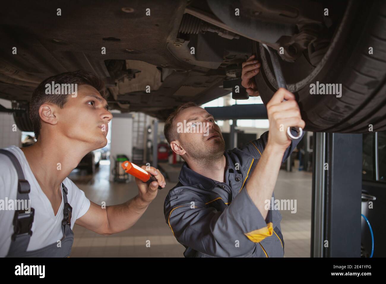 Two car mechanics working underneath a broken vehicle at the garage ...