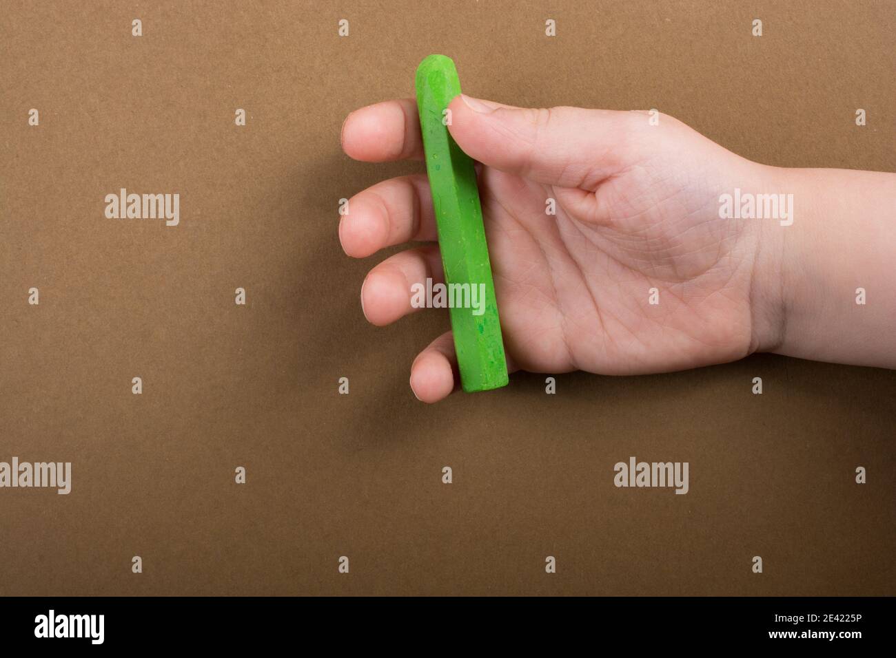 Closeup shot of a child holding a green crayon by a brown background ...