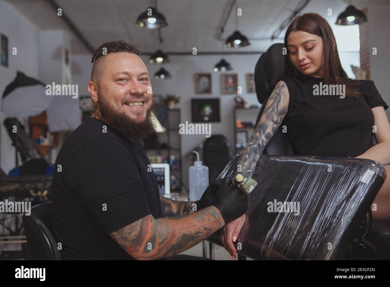 Cheerful bearded tattooed man smiling to the camera over his shoulder ...