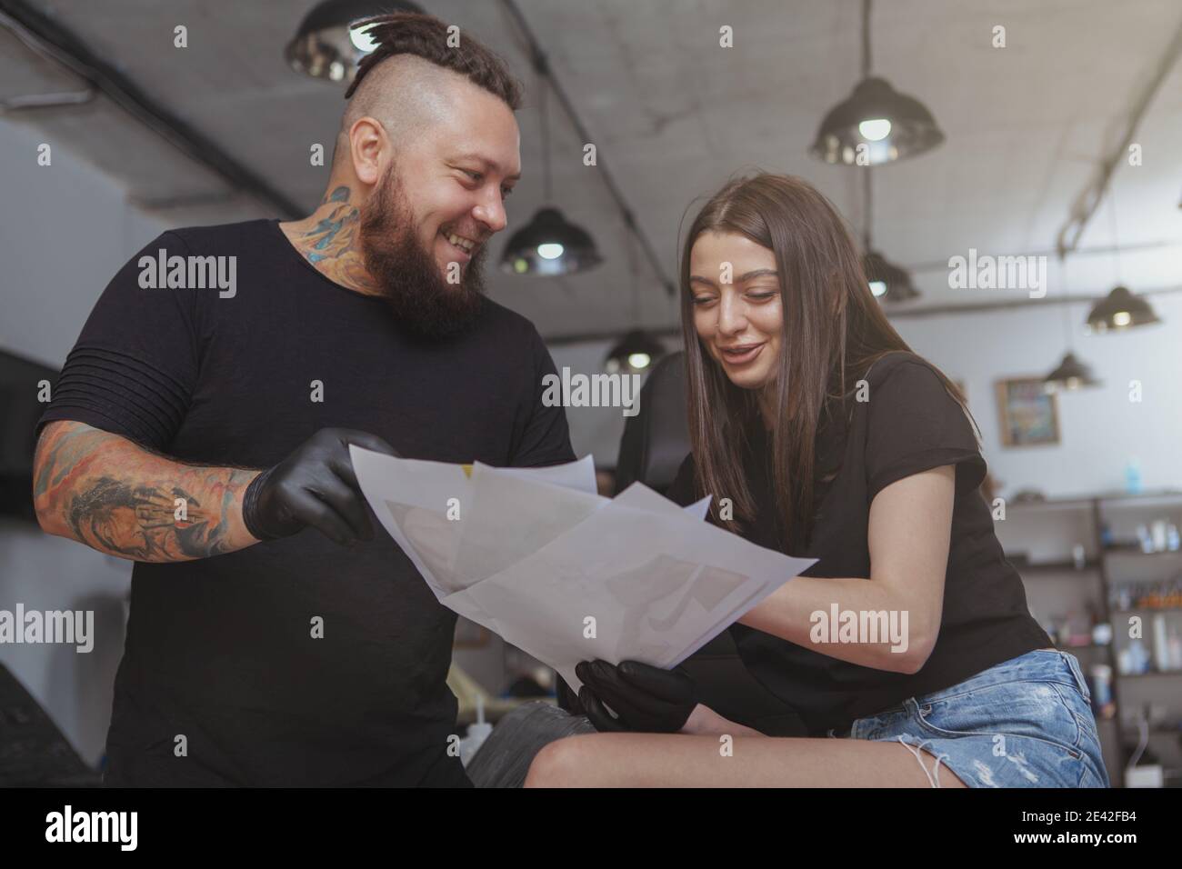 Cheerful bearded tattoo artist laughing, talking to his female client ...