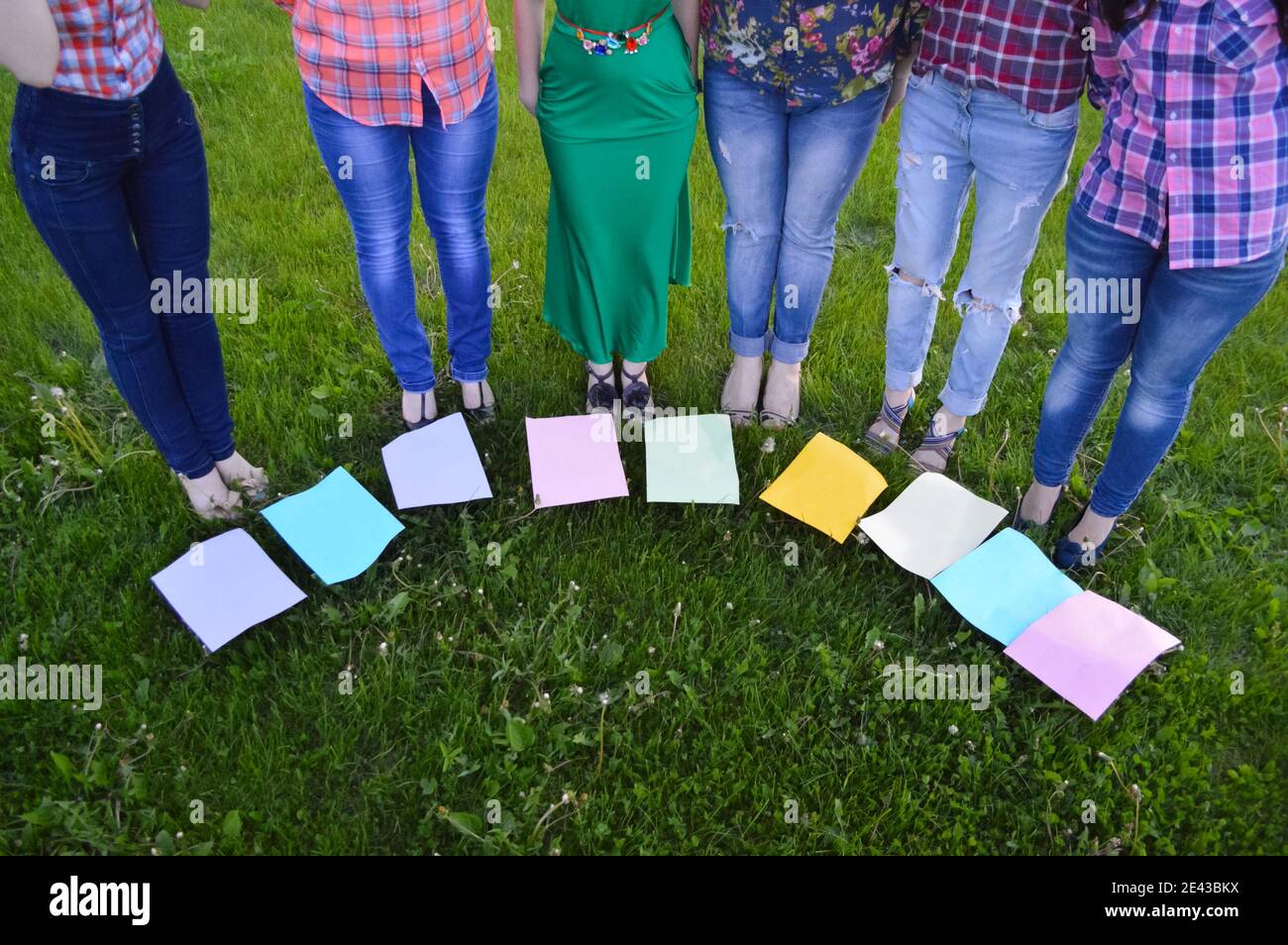 Women stand on the lawn in a semicircle. There are pieces of paper on ...