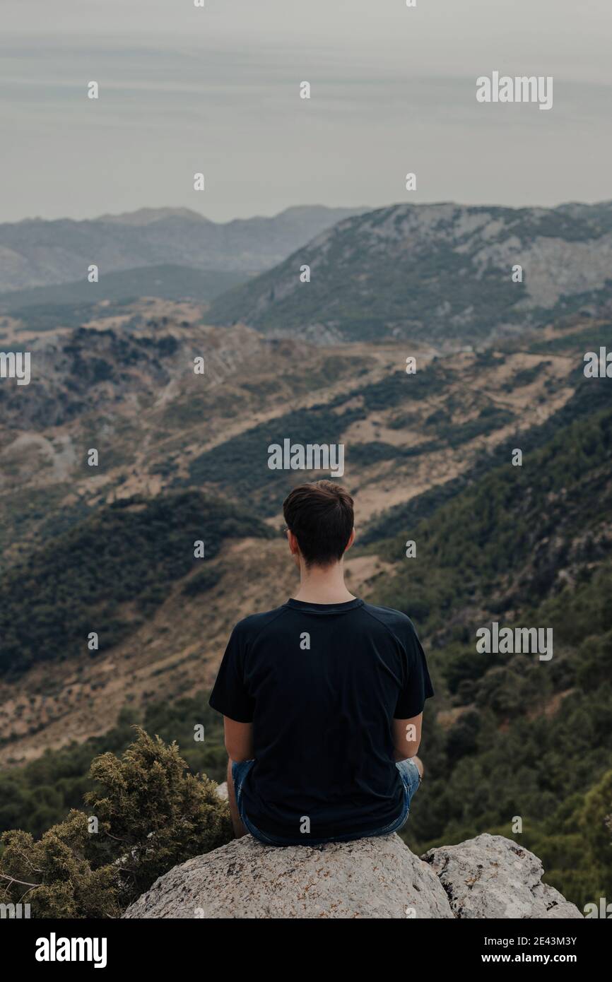 Back view of unrecognizable male hiker sitting on rocky slope of ...