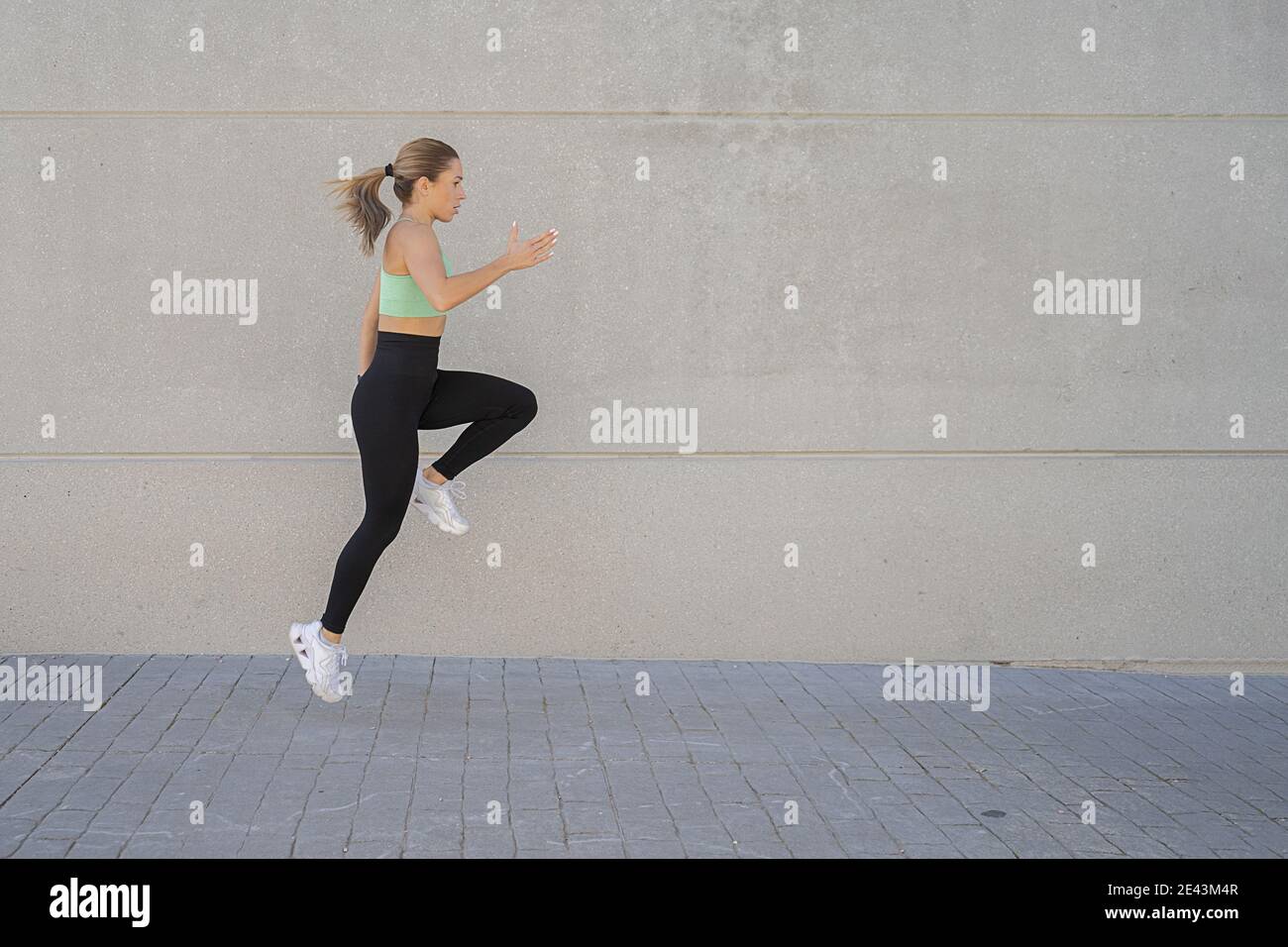 Side view of athletic Woman in activewear jumping above ground in ...