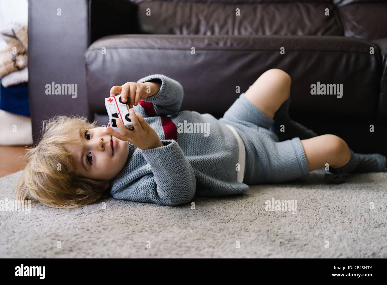 Cute little boy lying on carpet and playing with toy car in living room ...