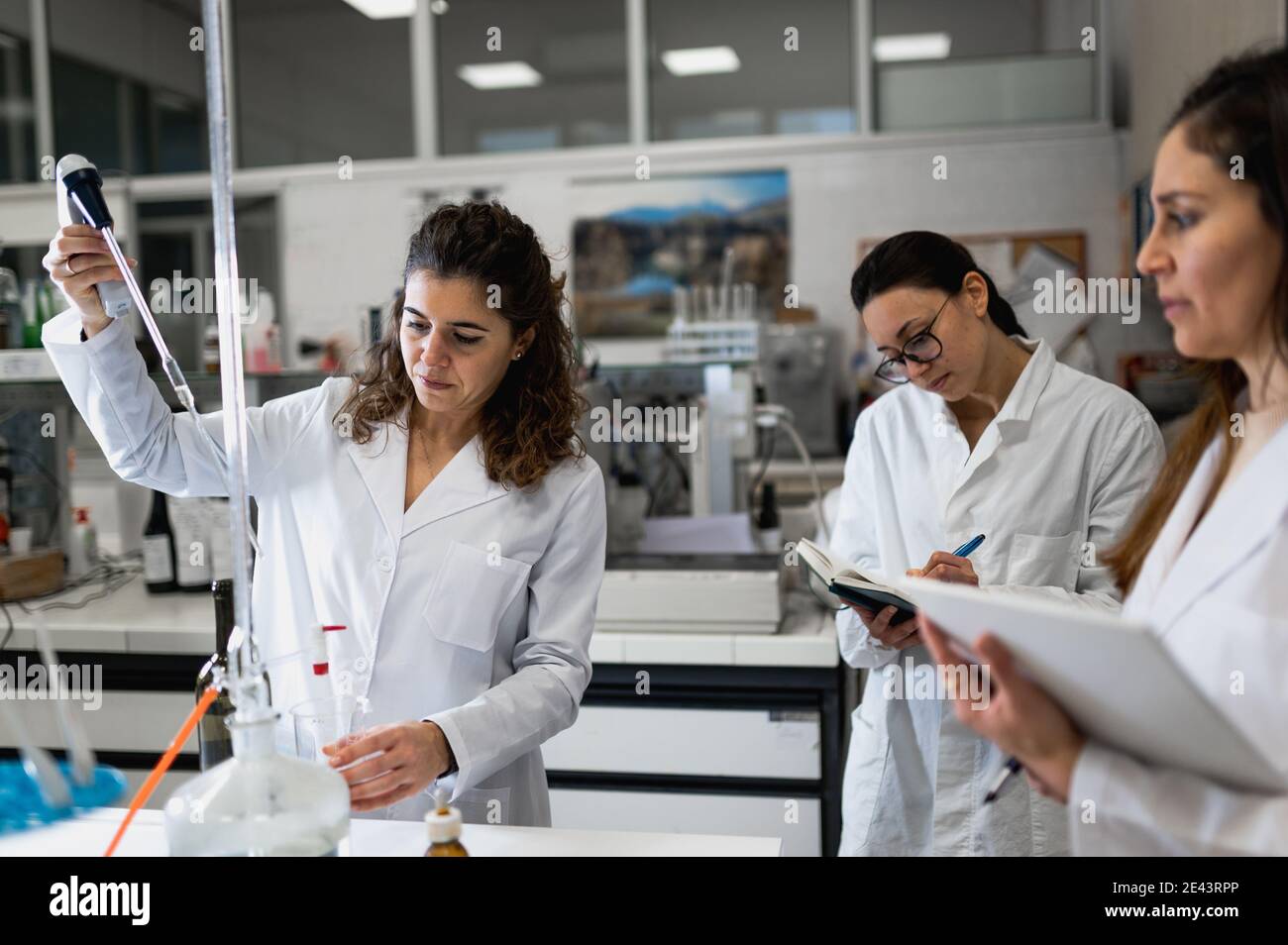 Group of female scientists in white coats examining results of chemical ...