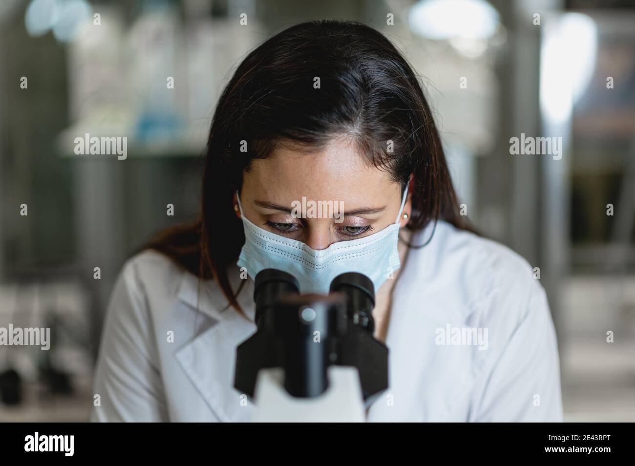 Skilled female scientist in protective mask using microscope while ...