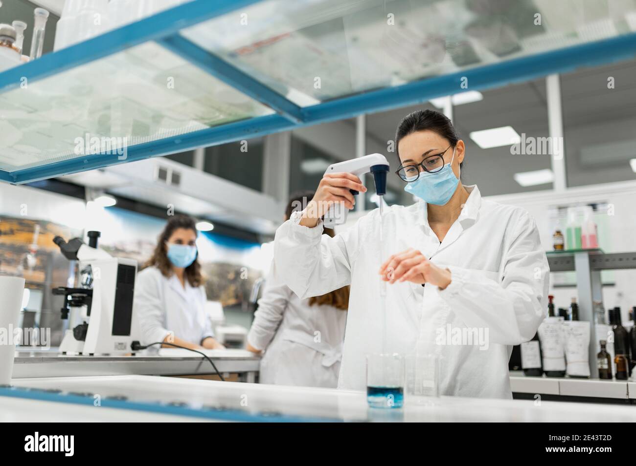 Professional female scientist in white coat and protective mask ...