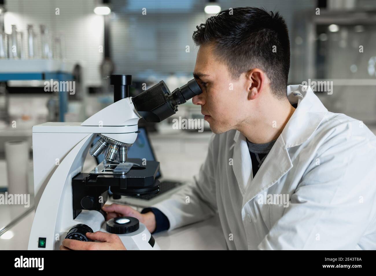 Side view of skilled male scientist using microscope while conducting ...
