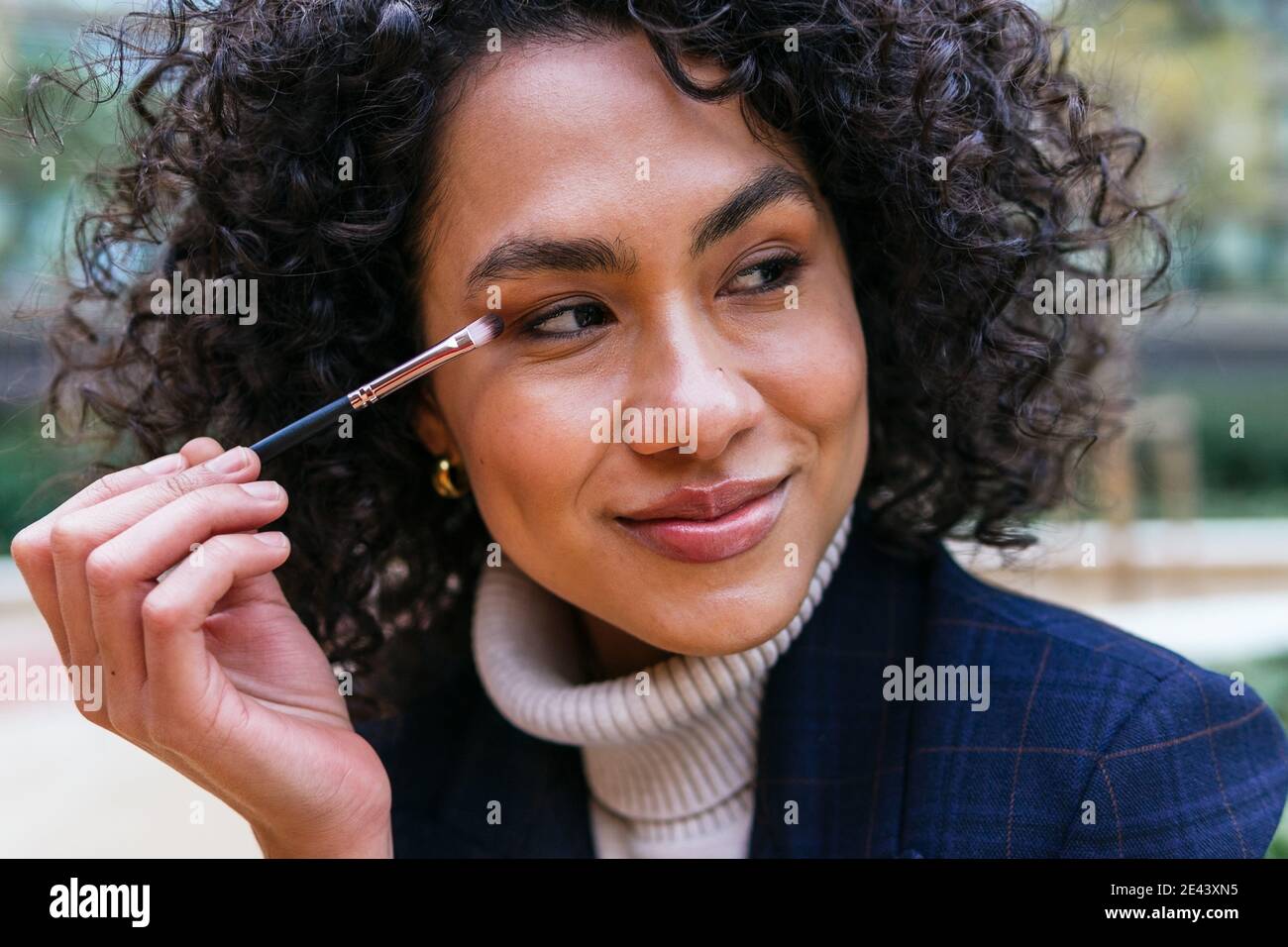 Charming smiling African American female applying eyeshadows with ...