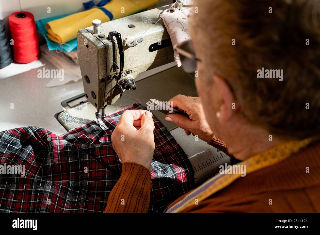 High angle back view of senior female dressmaker cutting thread with ...