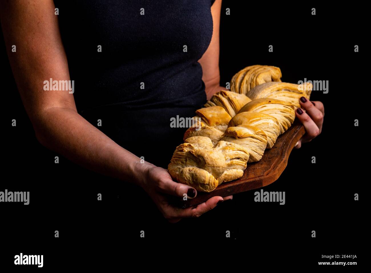 Crop female baker holding wooden board with puff braided bun of bread ...