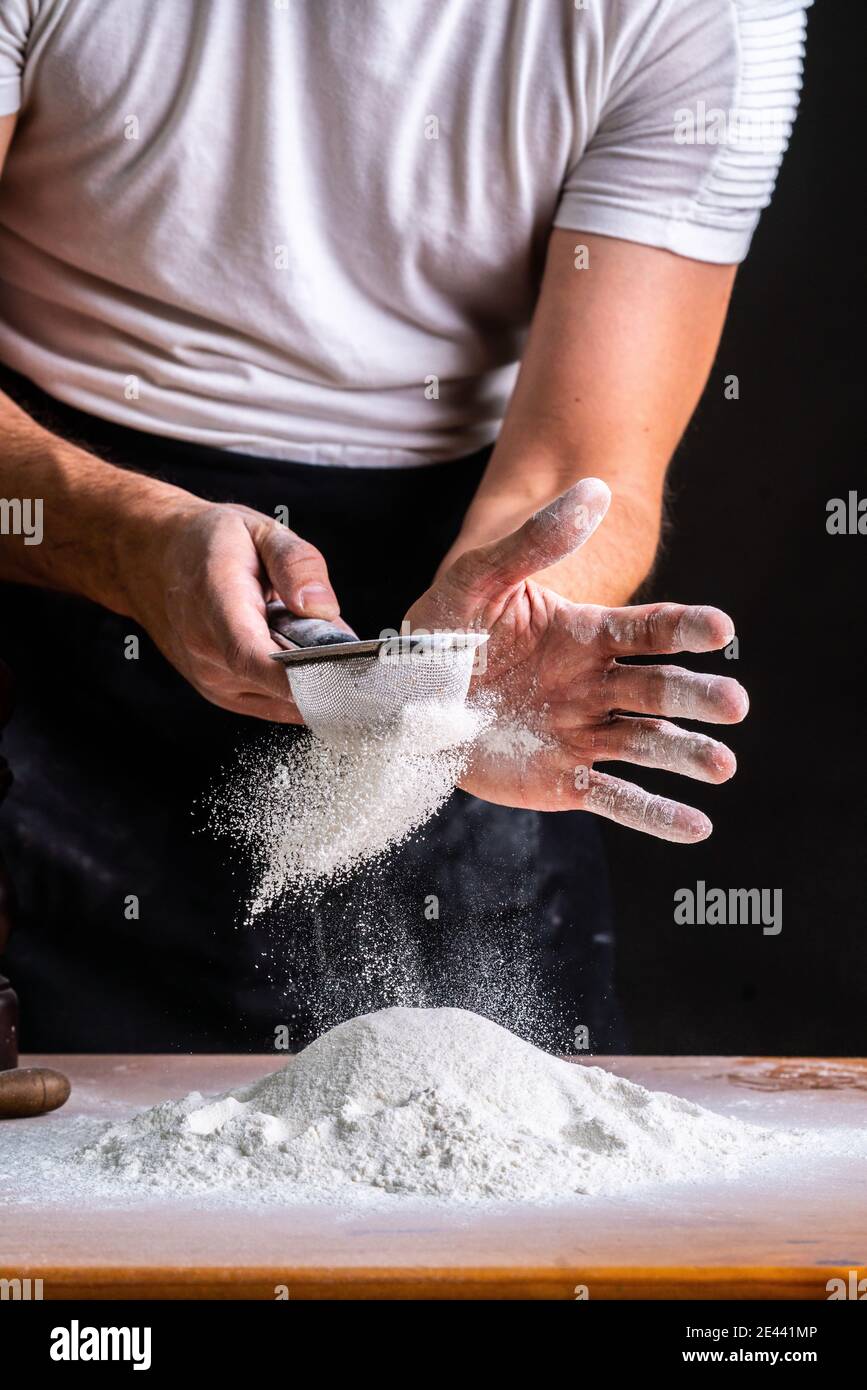 Faceless male baker sifting wheat flour with small sieve standing at ...