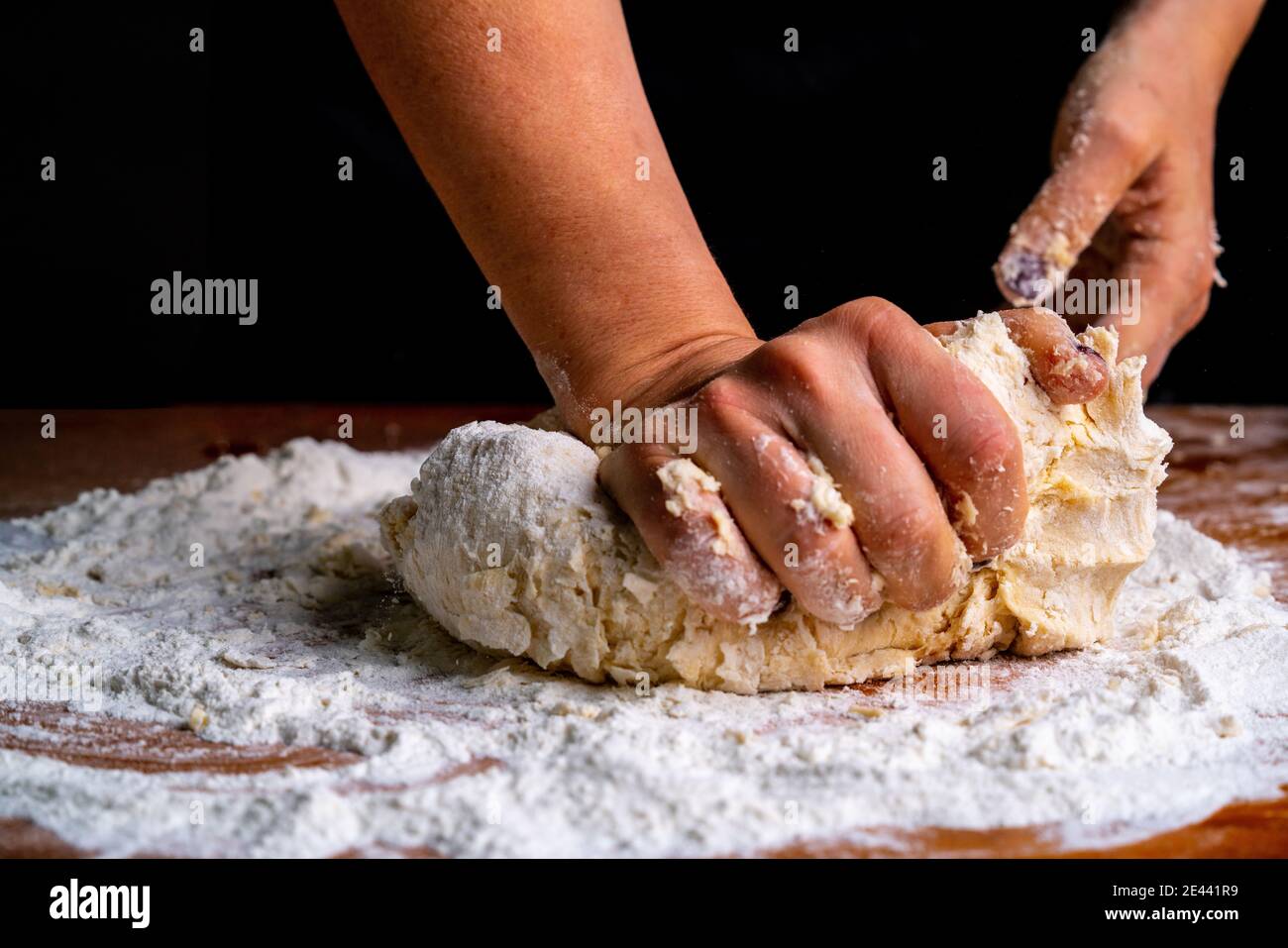 Crop Woman at wooden table kneading and rolling pile of dough for bread ...