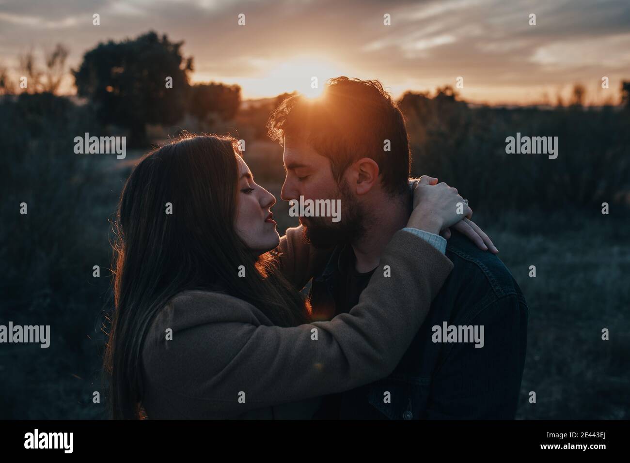 Tender couple kissing with closed eyes while standing in field with ...