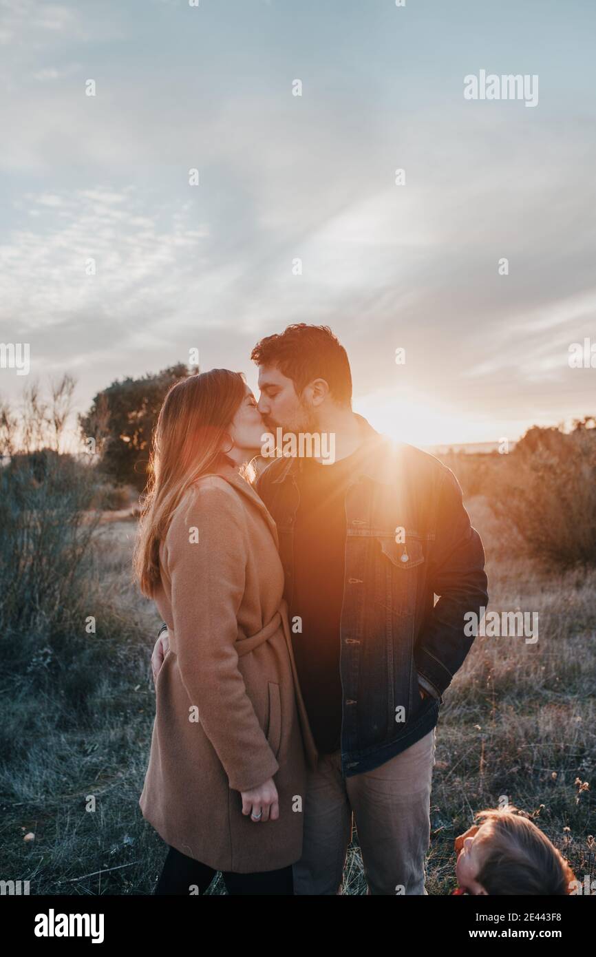 Tender couple kissing with closed eyes while standing in field with ...