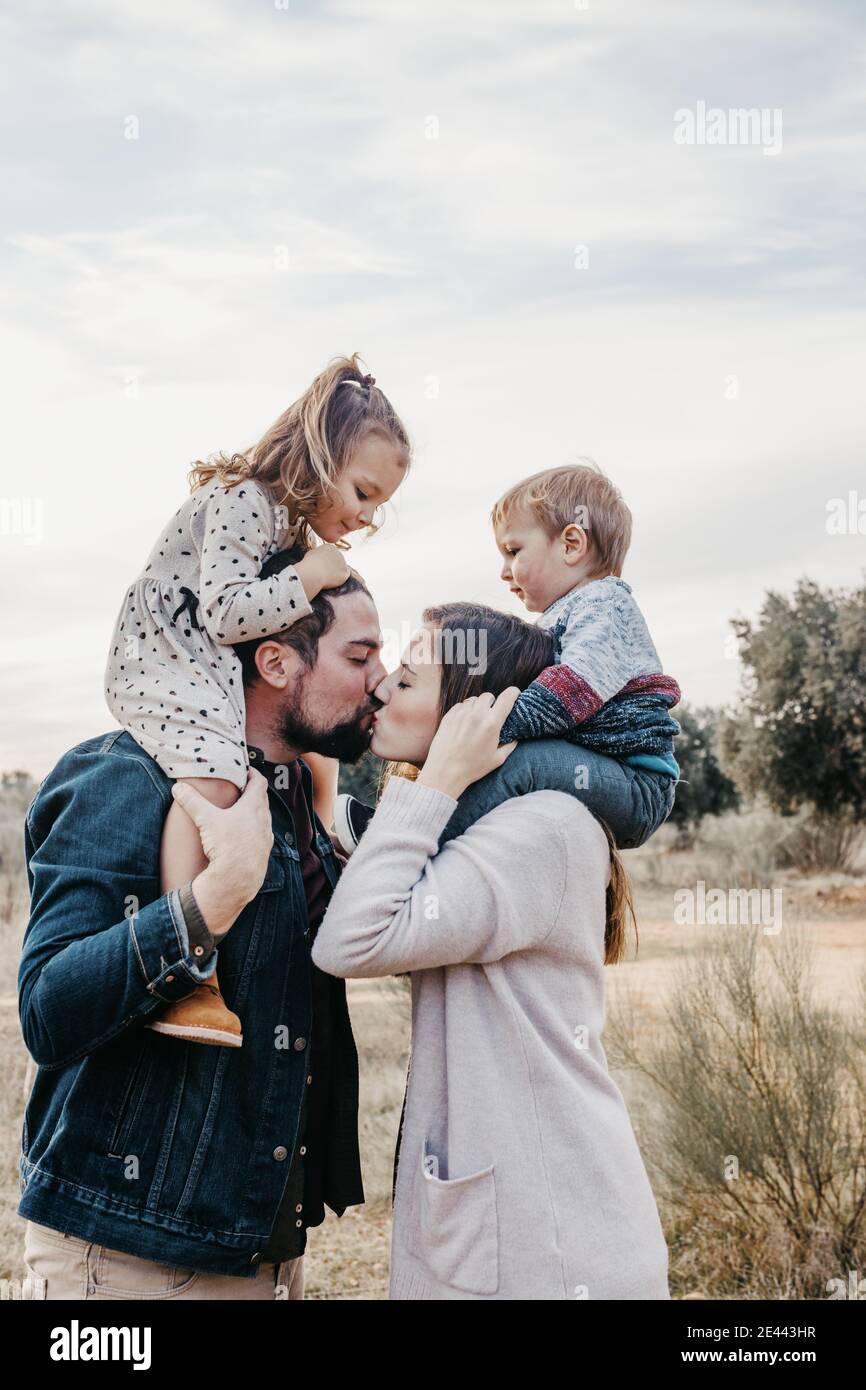 Side view of loving couple with children on shoulders kissing tenderly ...